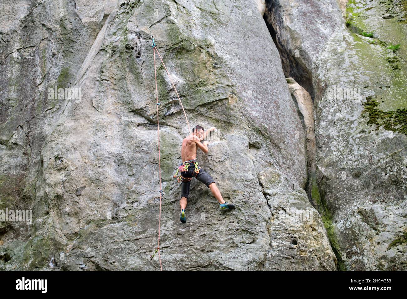 Young man climbing steep wall of rocky mountain. Male climber overcomes ...