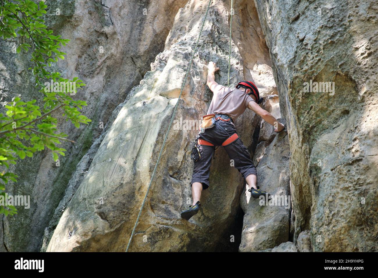 Young man climbing steep wall of rocky mountain. Male climber overcomes ...