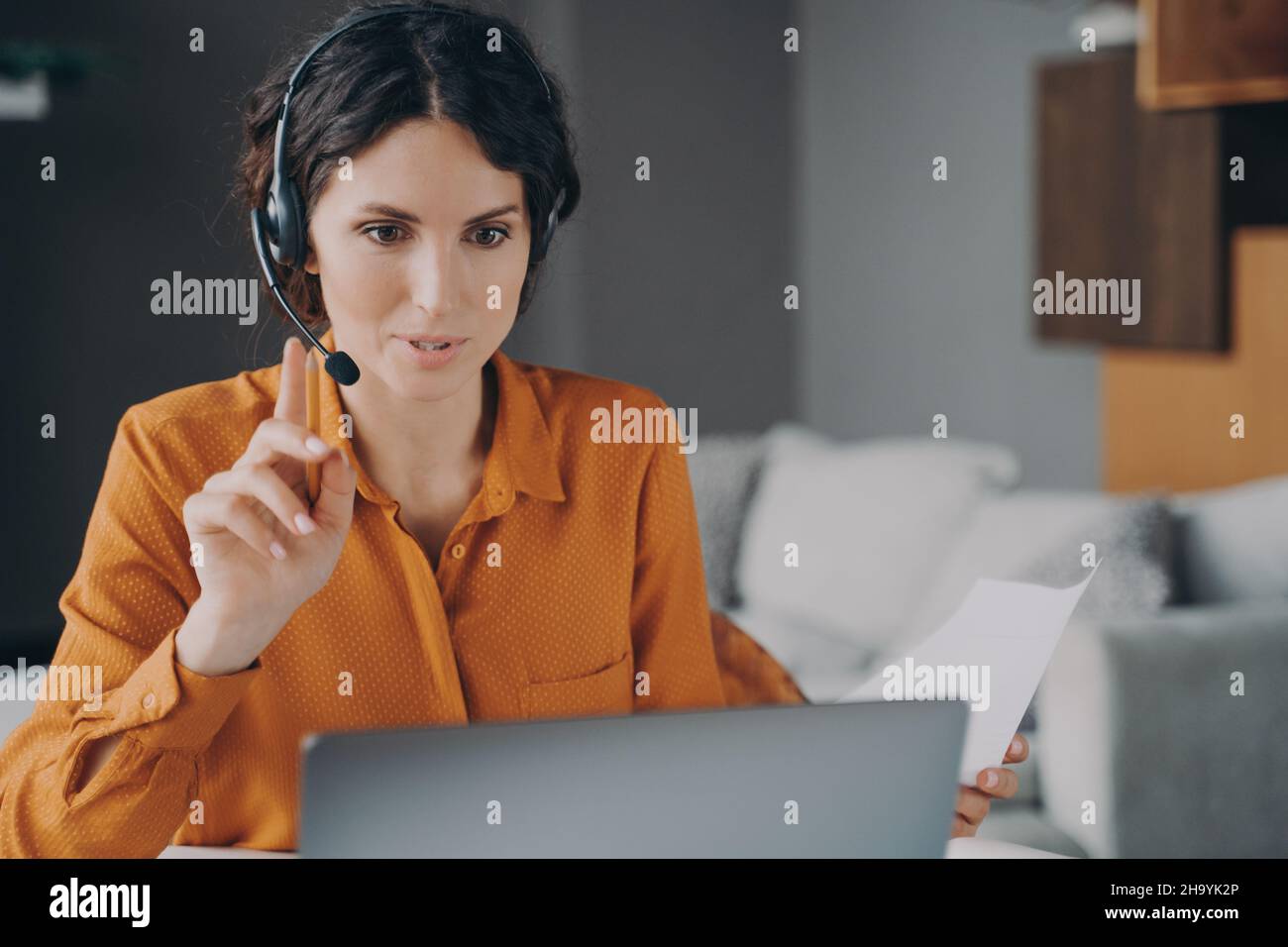 Young Spanish woman tutor wearing headset looking at laptop screen ...