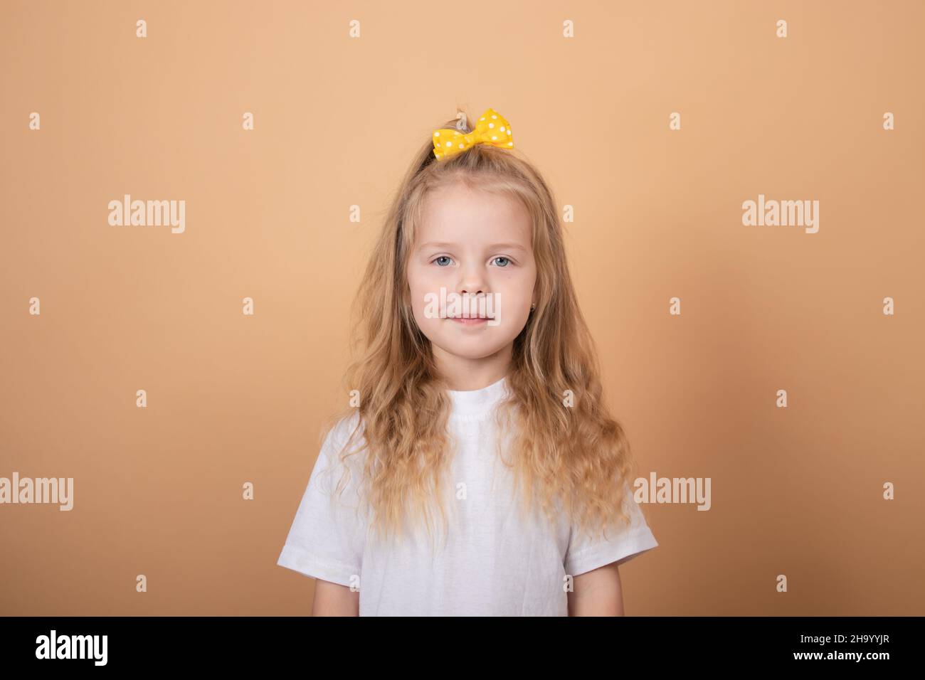 adorable blonde little girl in white t-shirt. on brown - yellow background. innocence child ...