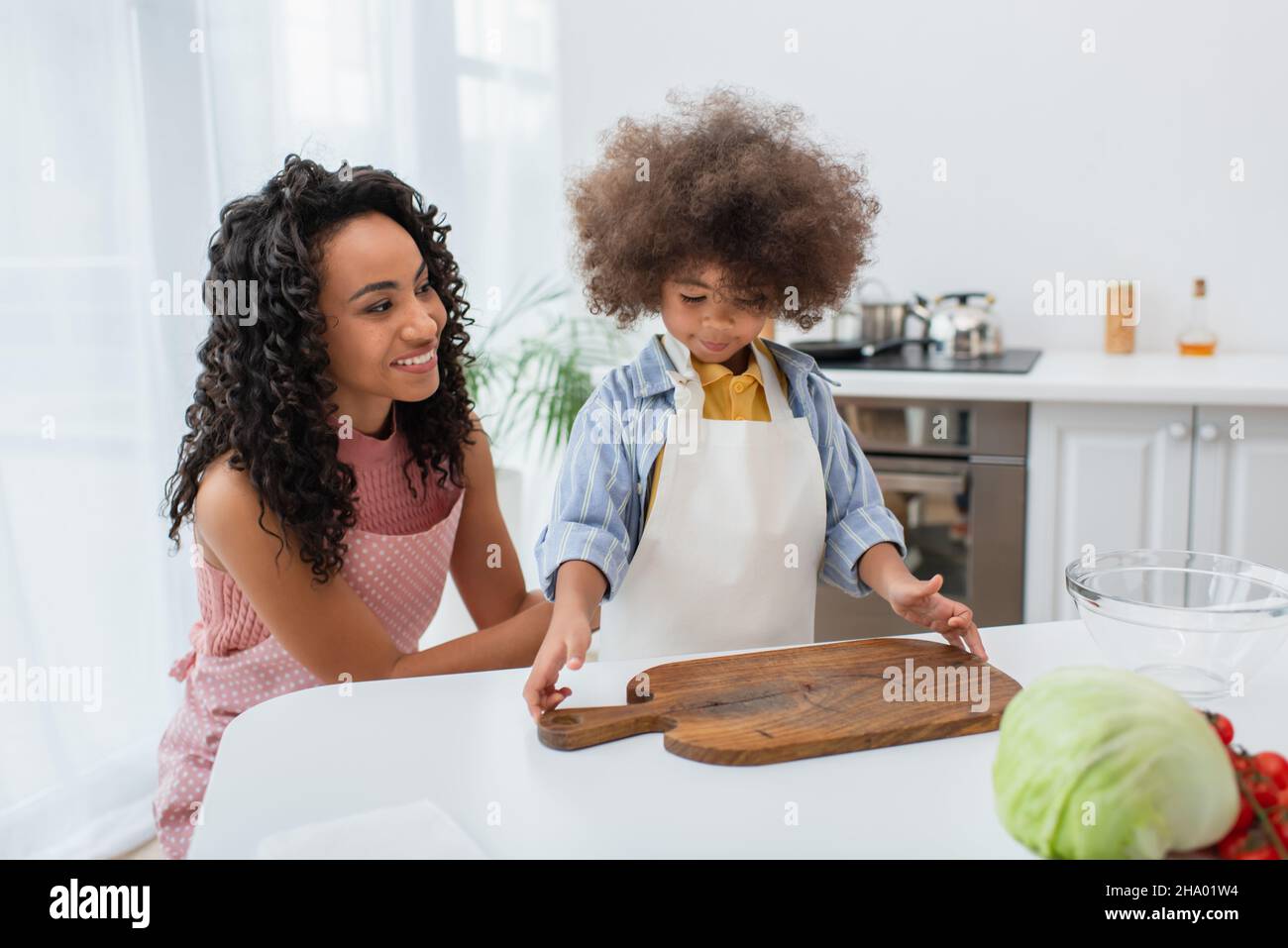 Positive african american mother in apron standing near daughter ...