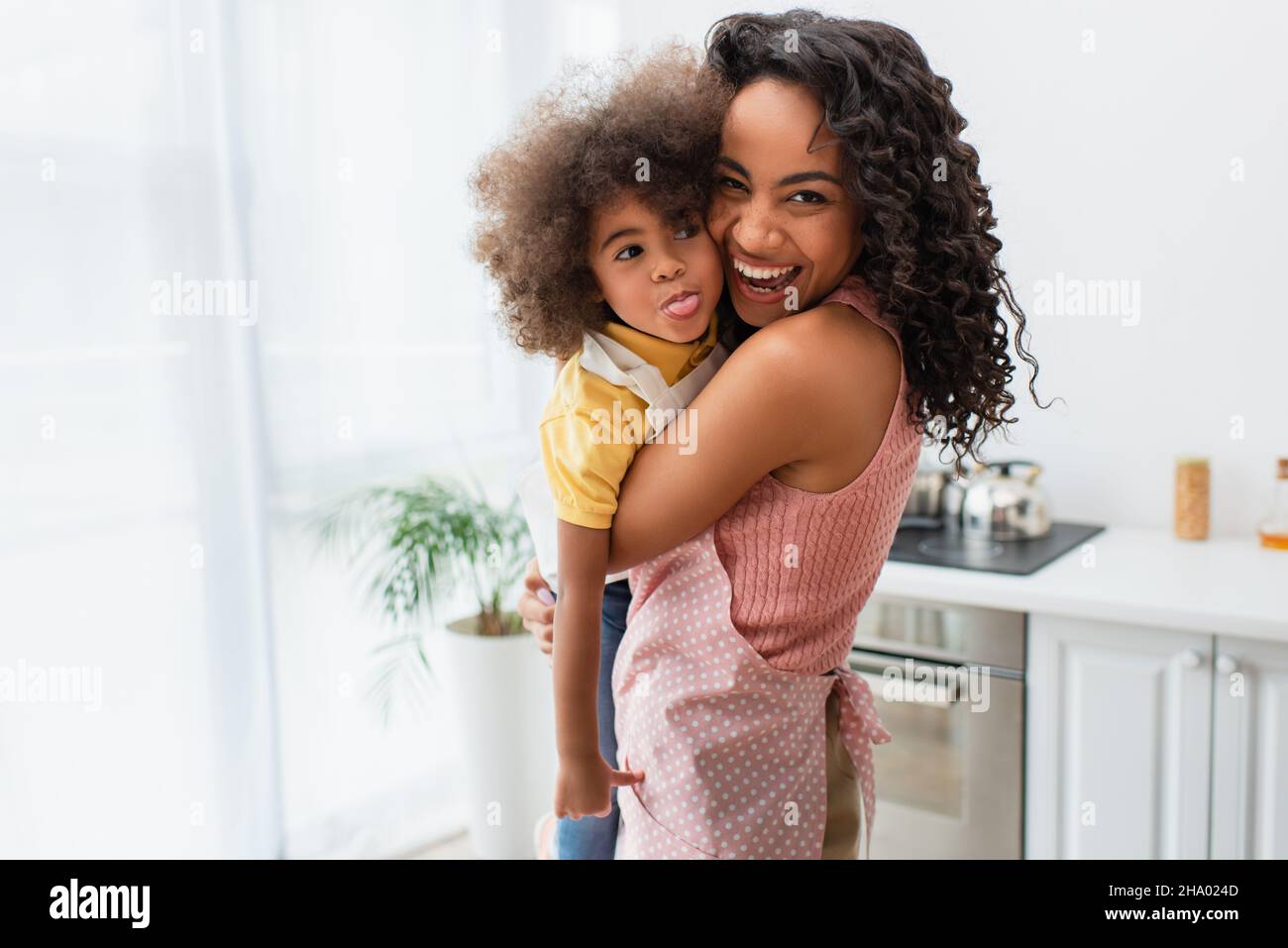 Happy african american mother in apron hugging child sticking out ...