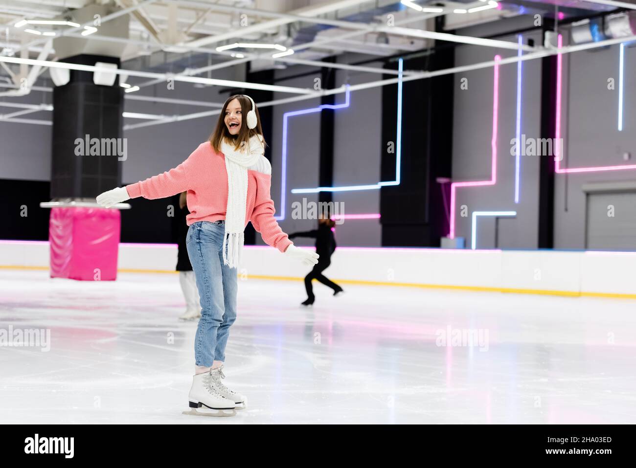 full length of cheerful young woman in winter outfit skating with ...