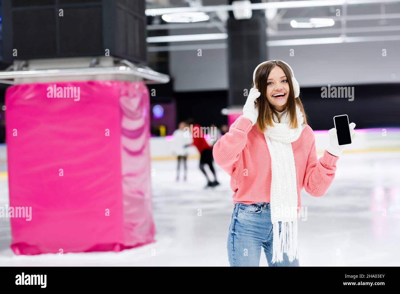 amazed woman in white ear muffs holding smartphone with blank screen on ...