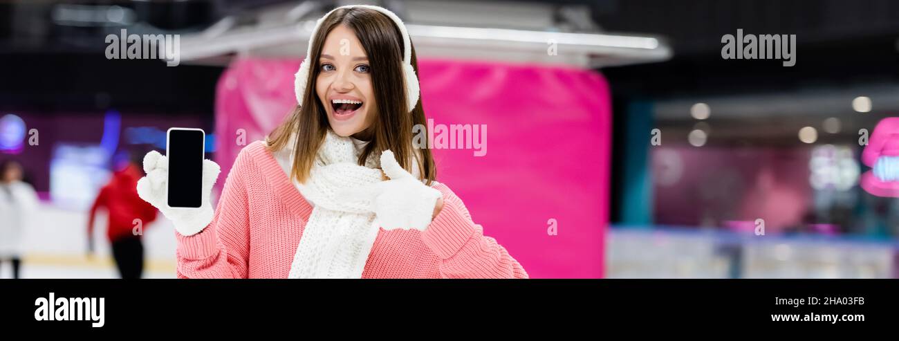 happy woman in ear muffs showing thumb up and holding smartphone with ...