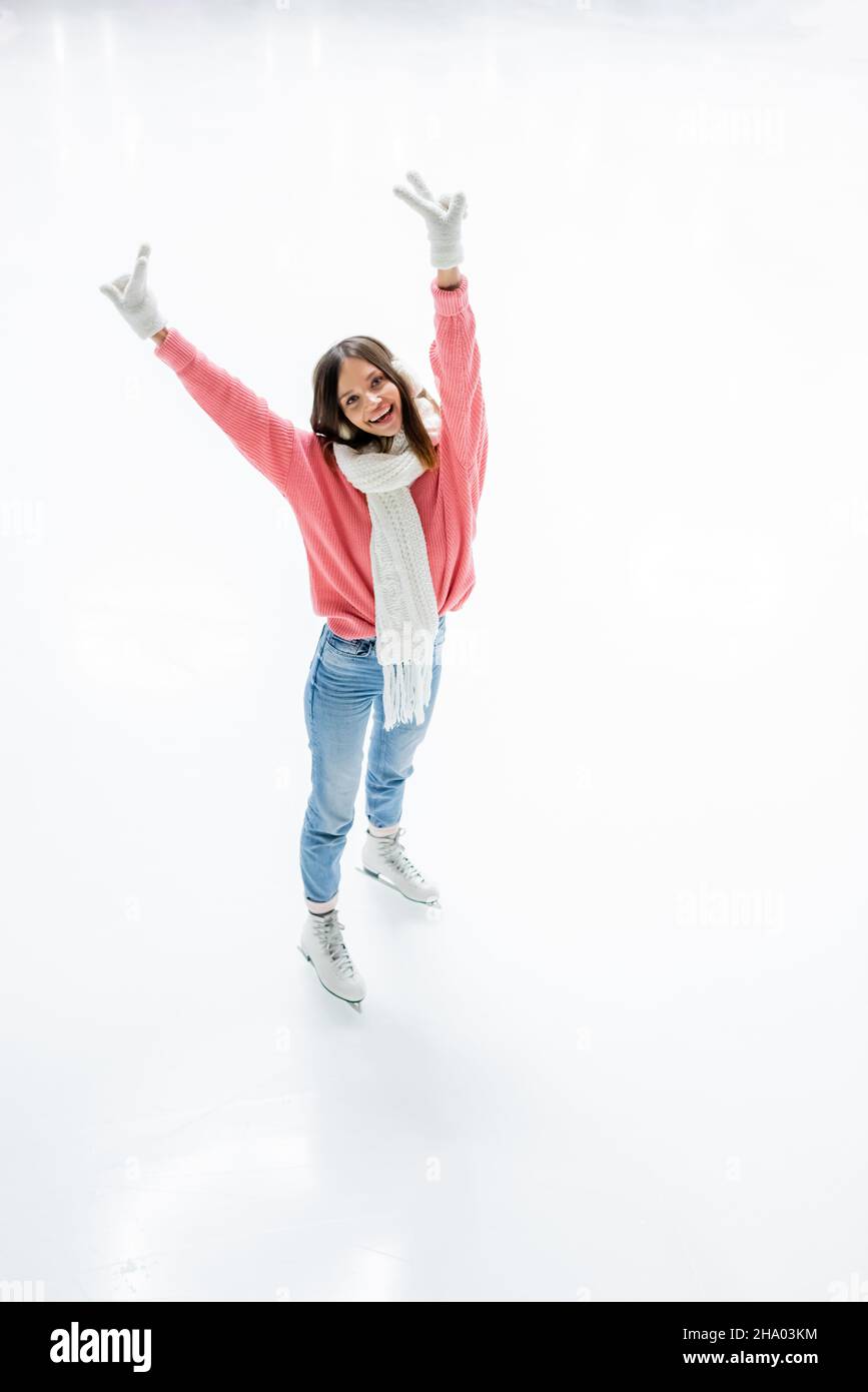 high angle view of cheerful young woman in ear muffs and scarf showing ...