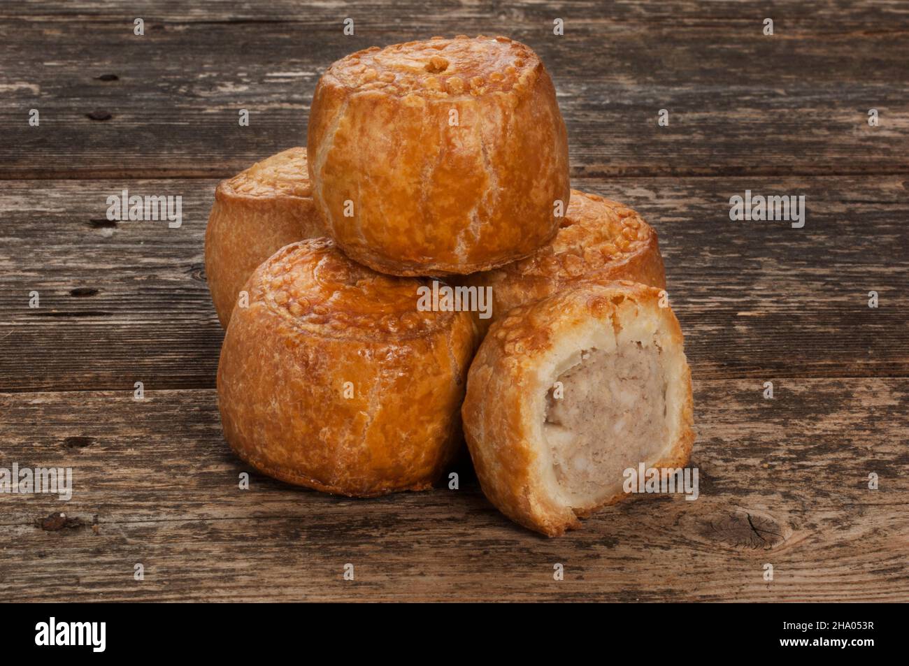 Studio shot of small pork pies resting on a dark wooden board - John ...