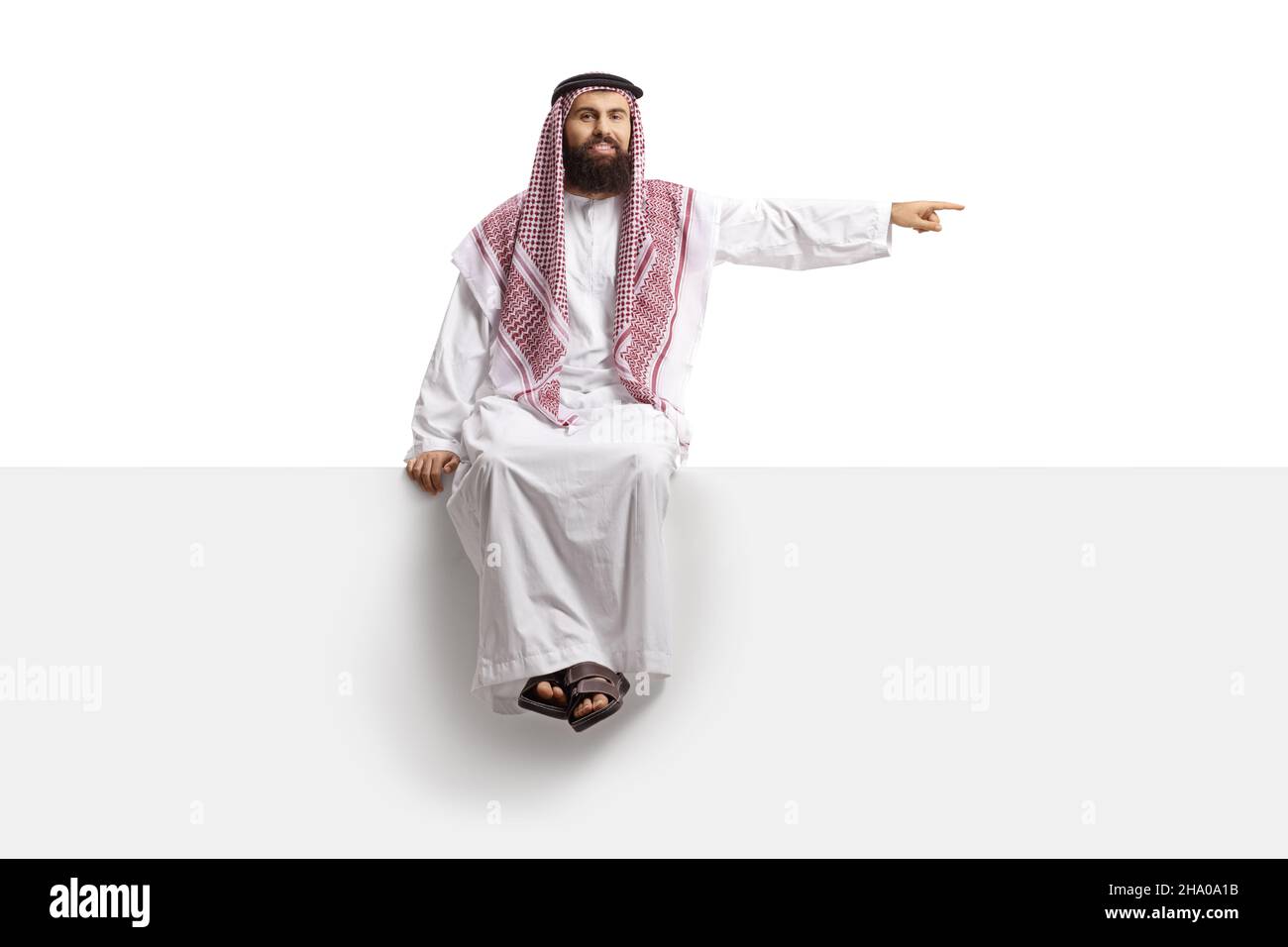 Saudi arab man sitting on a blank panel and pointing isolated on white ...