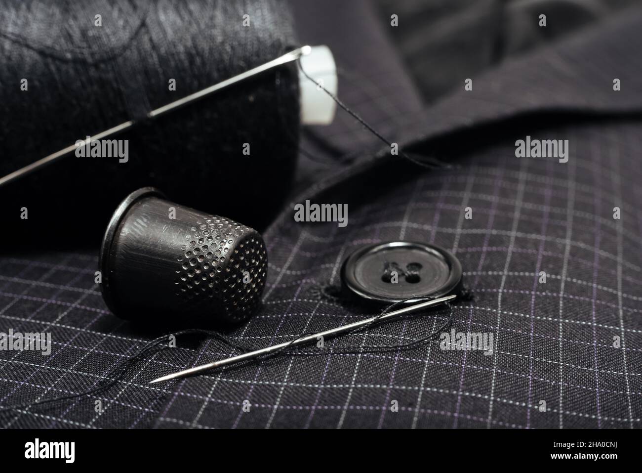 A needle and thread sews up a button on a plaid suit. Thimble. Textile ...