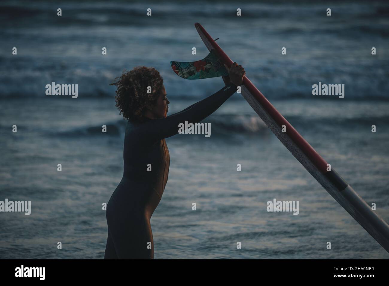 Woman carrying surfboard at sunset by pier Stock Photo - Alamy