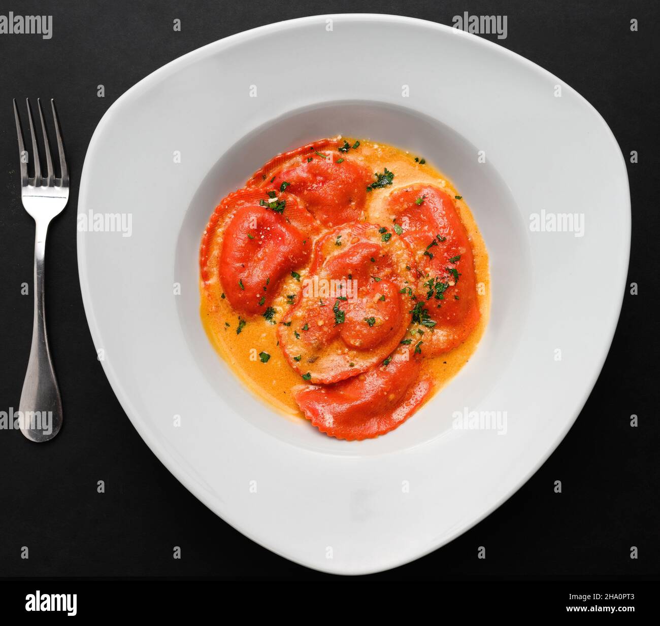 Red Ravioli in a white plate over a black background Stock Photo - Alamy