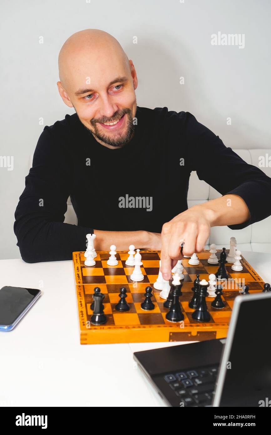 Bald man wearing beard playing chess on board near laptop. Strategy and ...