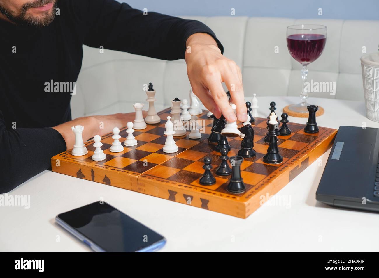 Thoughtful bald man wearing beard playing chess on board near laptop ...