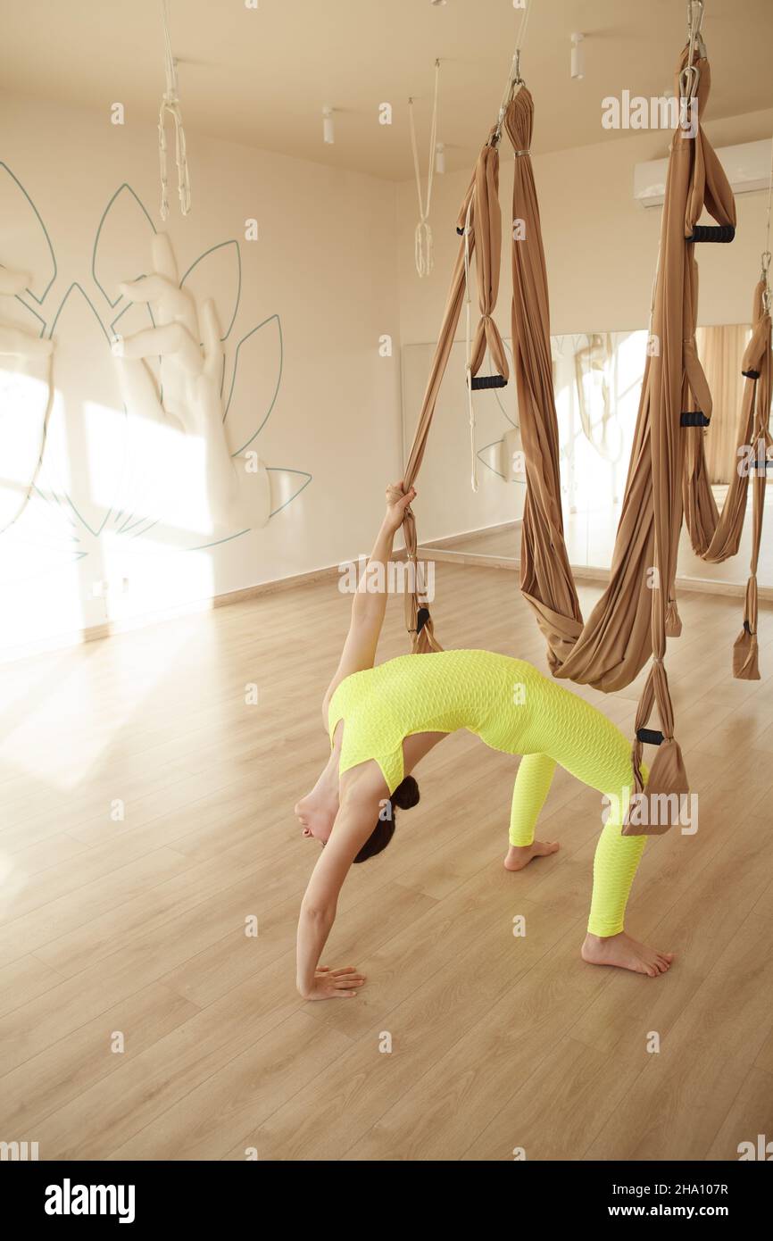 Vertical shot of female gymnast doing backbend exercise at aerial yoga ...