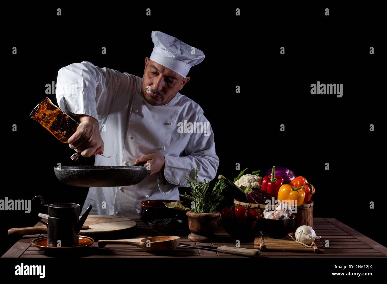 Male chef in white uniform pouring vinegar onto the cooking pan with ...