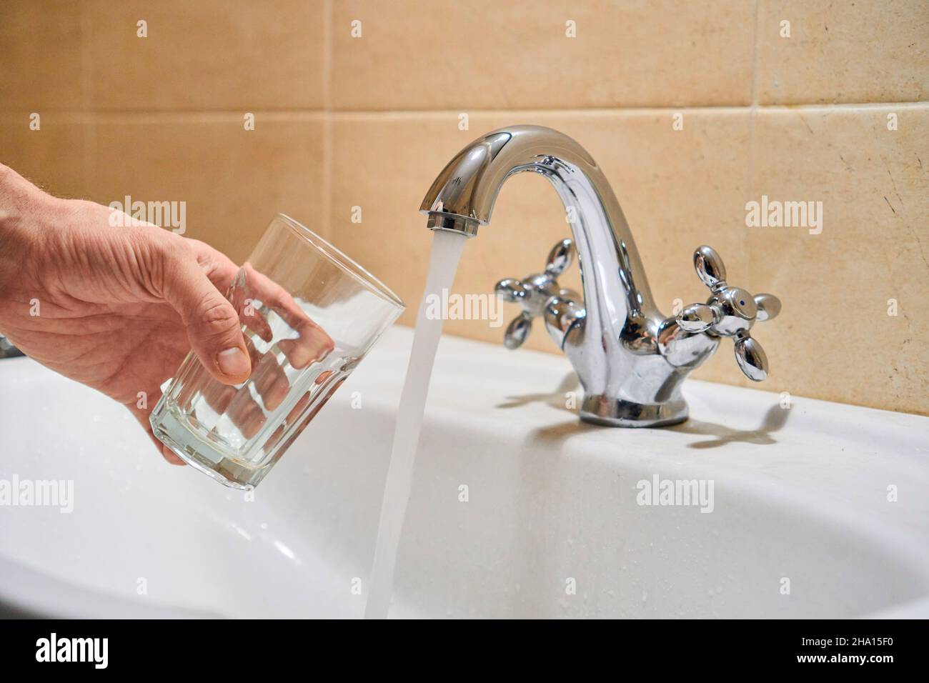 Mans hand holding empty glass nearby bathroom stainless steel pillar ...