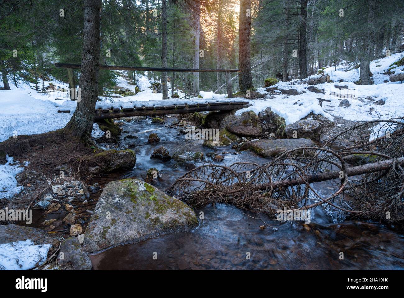 Snow covered small footbridge across a mountain creek in a snowy forest ...
