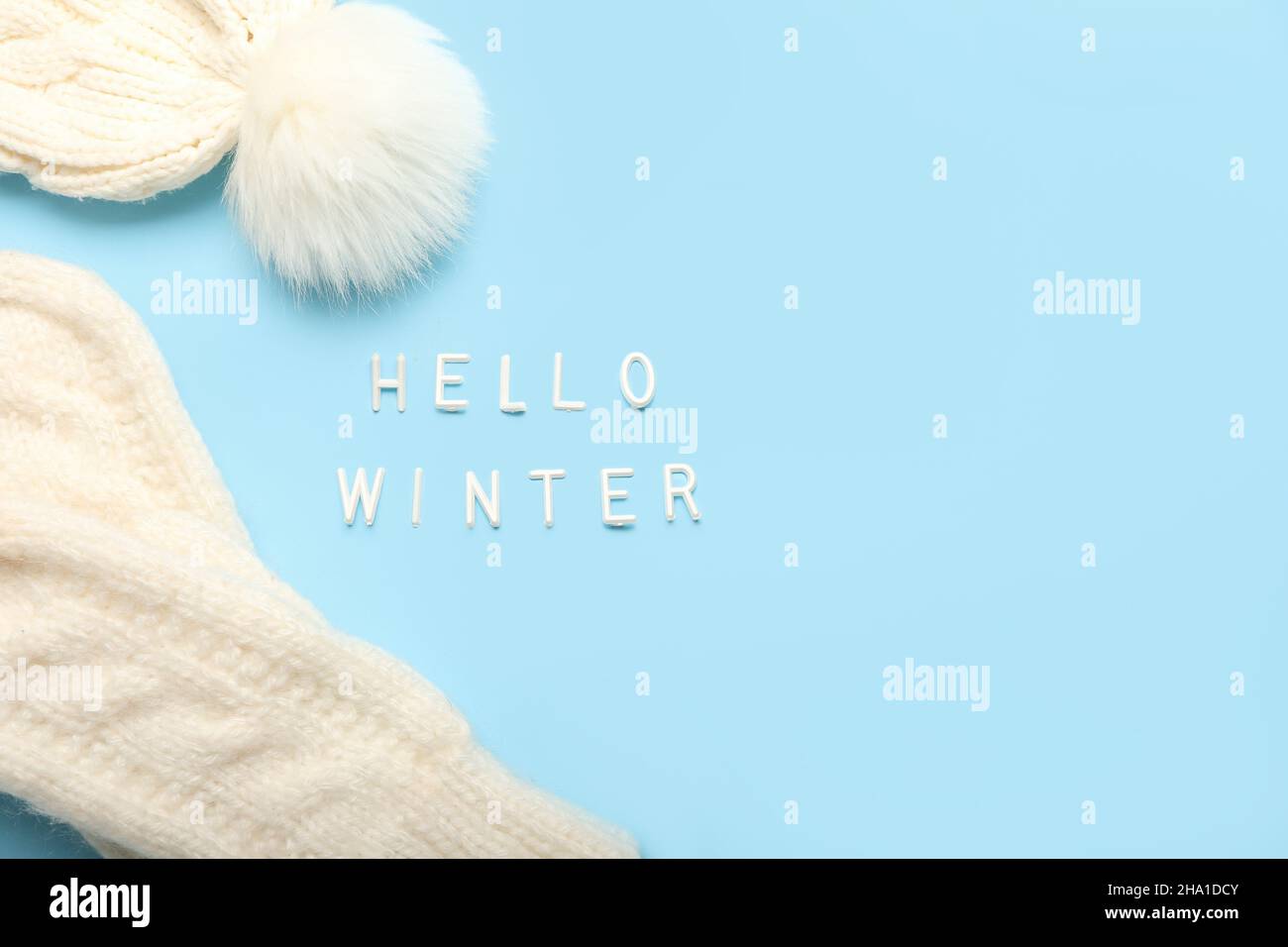 Text HELLO WINTER, knitted mittens and hat on color background, closeup ...