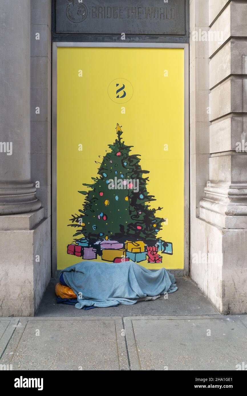 Homeless person sleeping on the street next to a Christmas Tree poster ...