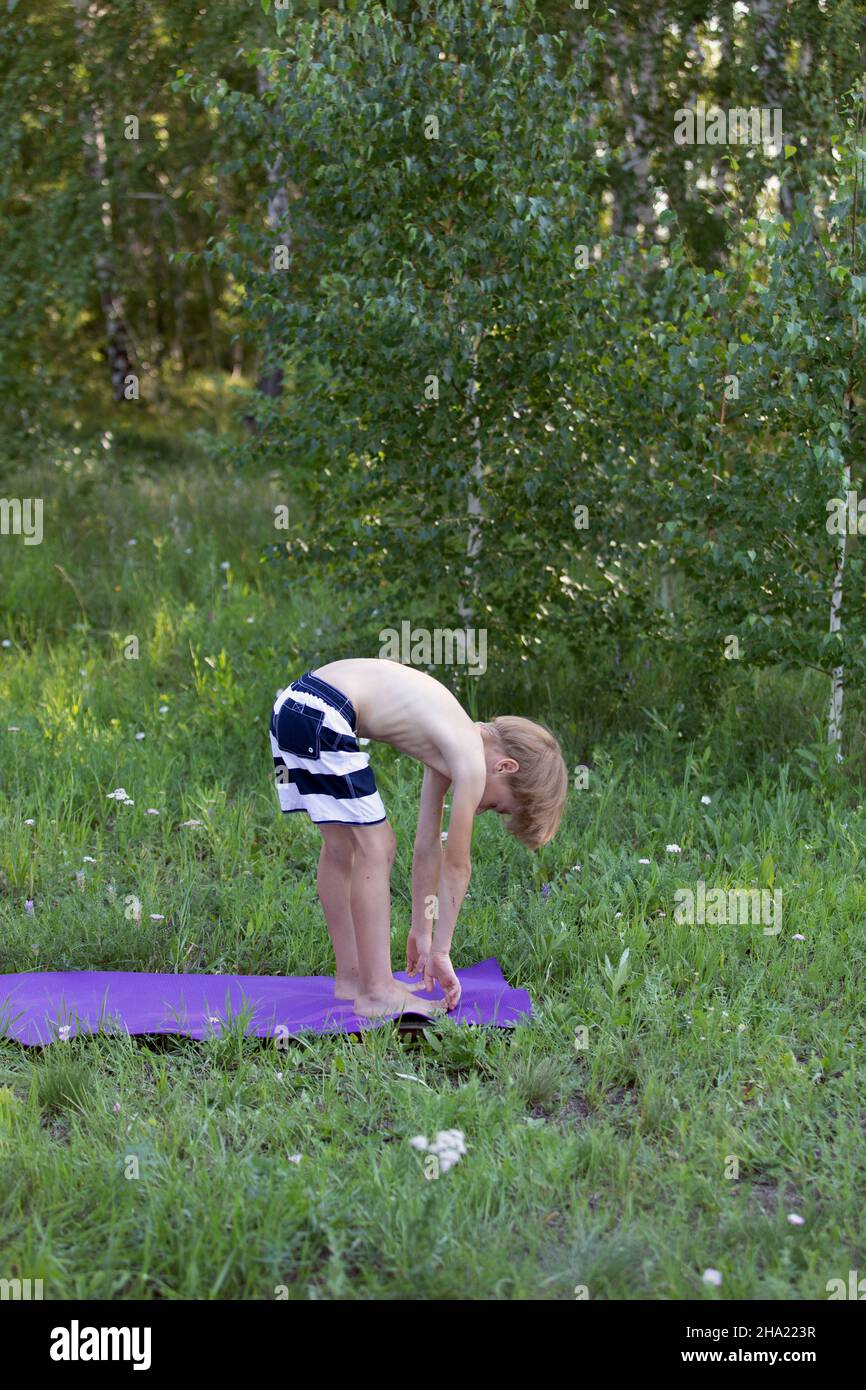Boy child in park is practicing yoga. Schoolboy doing Standing Forward ...