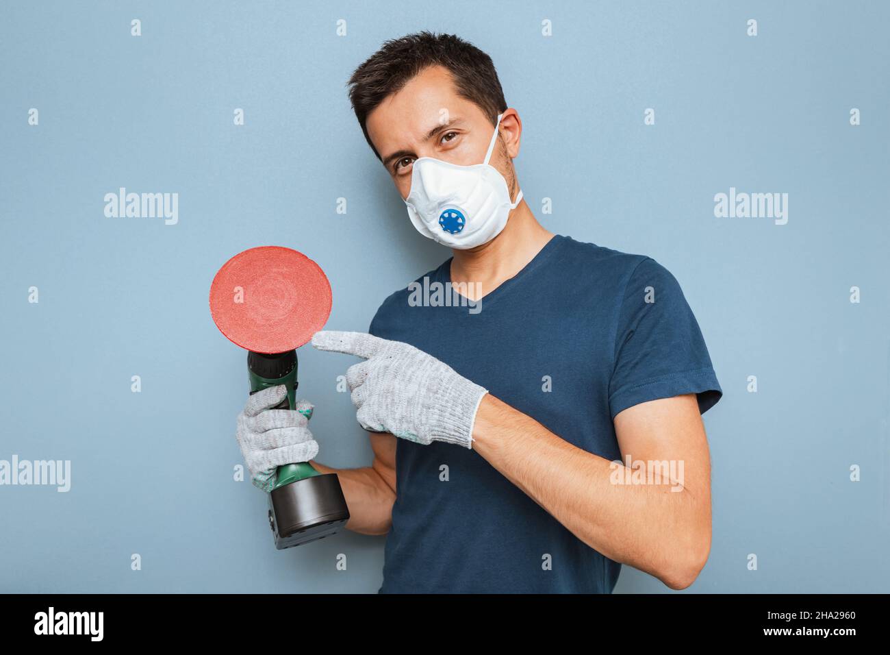 Young handyman wearing respirator grinding wall with disc sanding ...