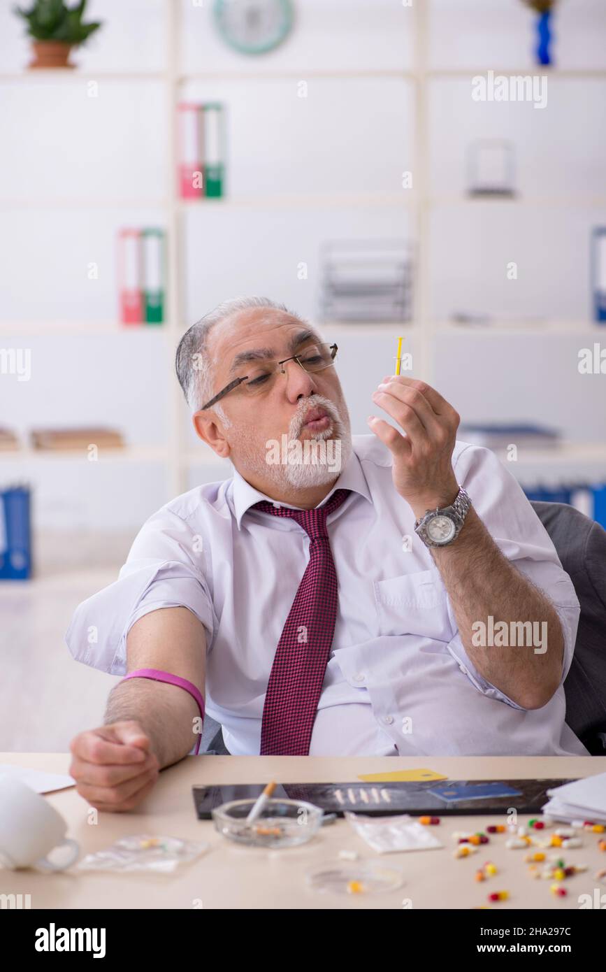 Old male drug addicted employee sitting at workplace Stock Photo - Alamy