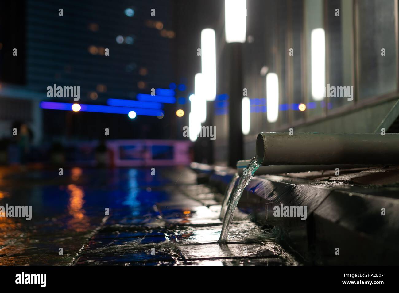 Water pours through drainage pipes near a modern building at night in ...