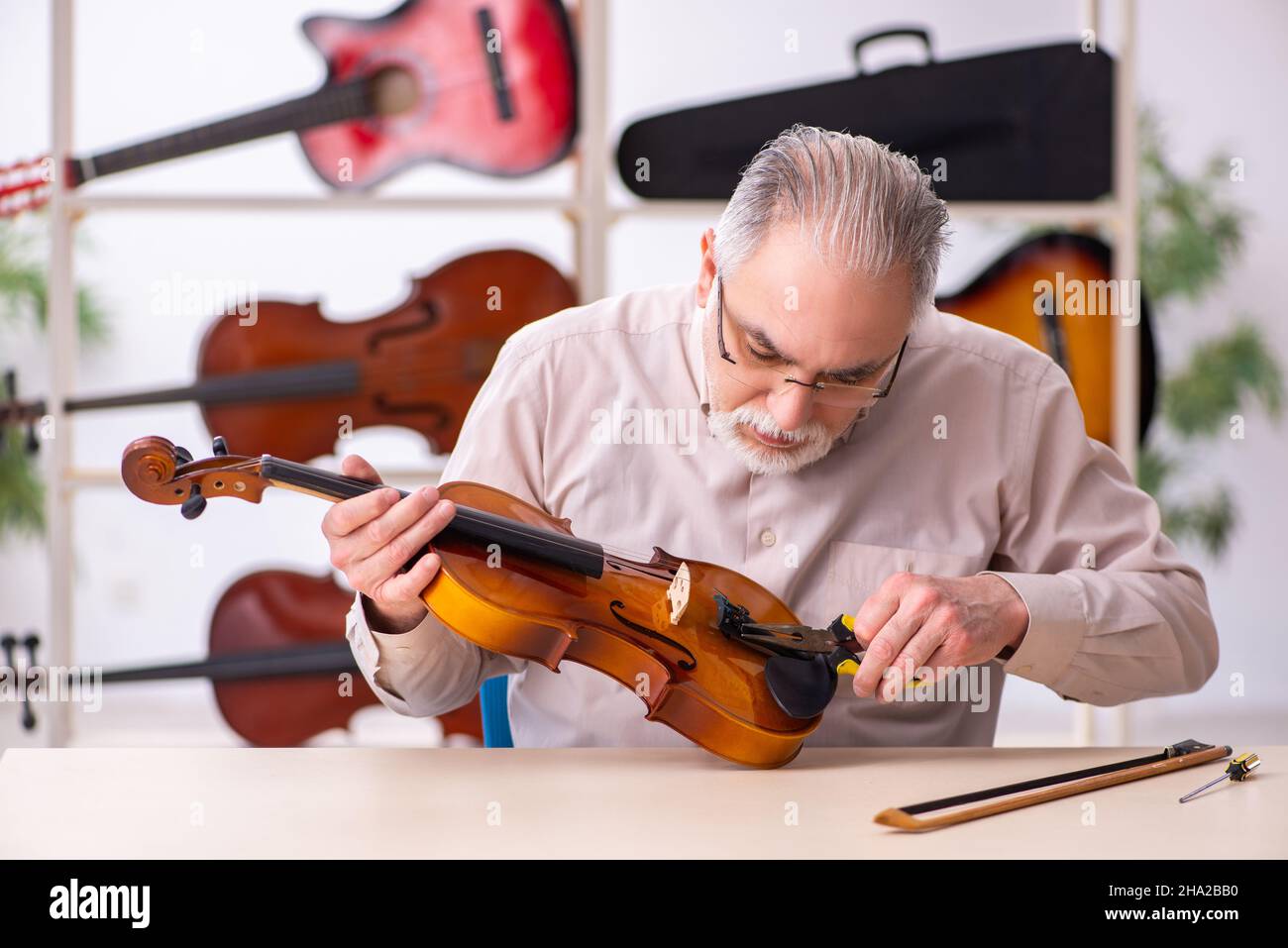 Old repairman repairing musical instruments at workplace Stock Photo ...
