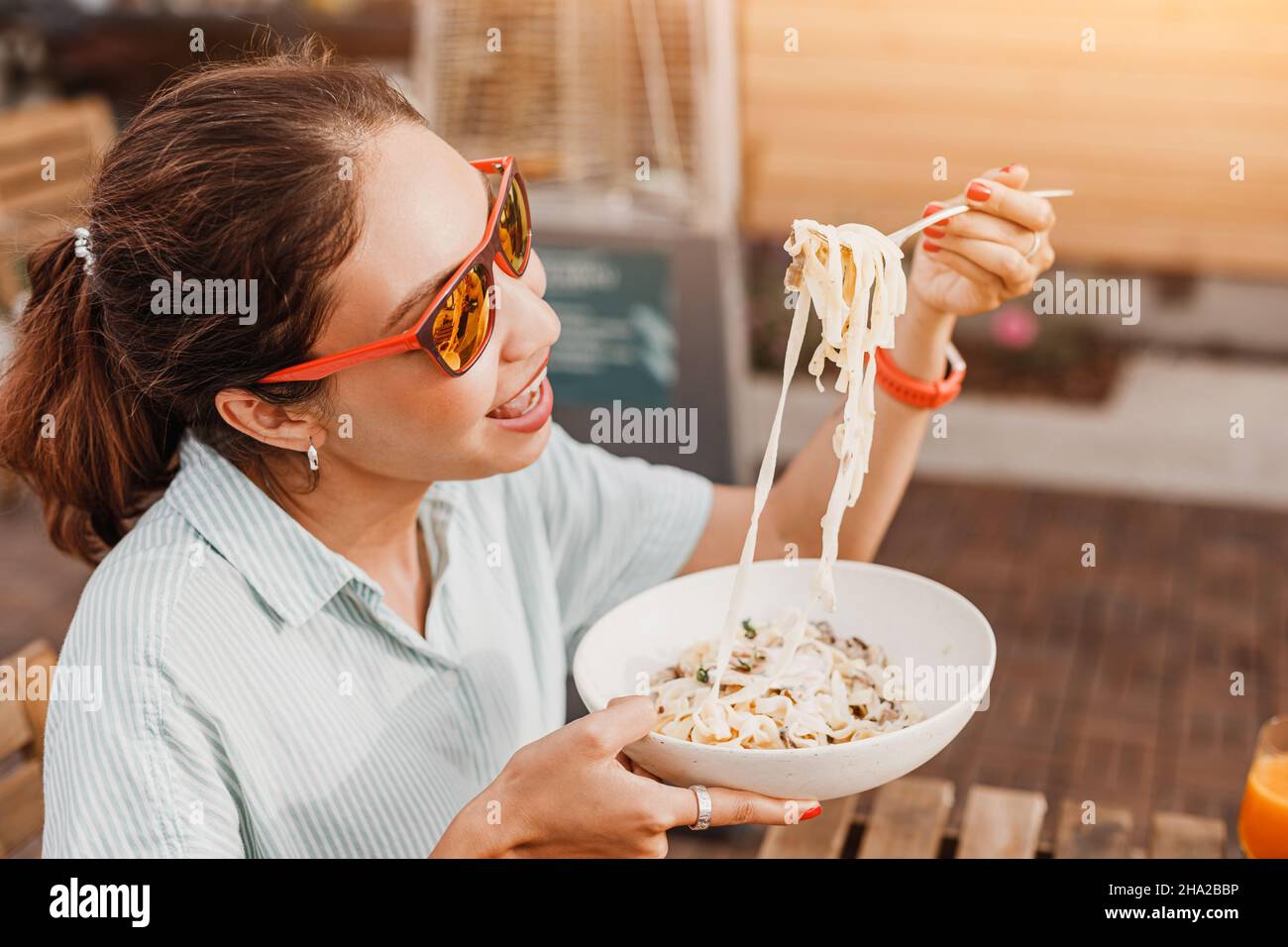 Happy asian woman eating itallian spaghetti or pasta outdoors in open ...