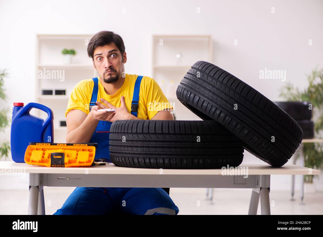 Young garage worker with tyre at workshop Stock Photo - Alamy