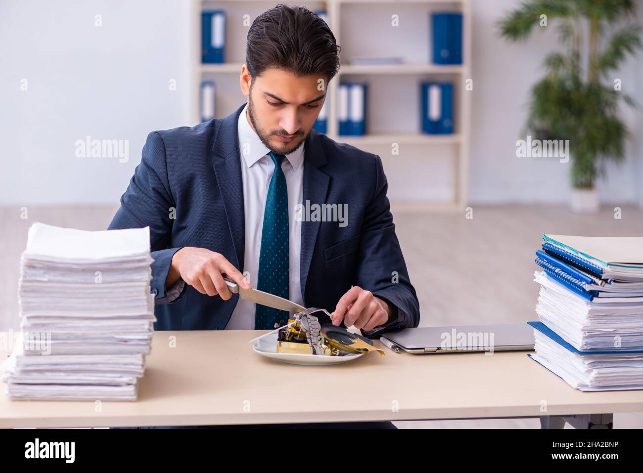 Young male employee eating alarm-clock Stock Photo - Alamy