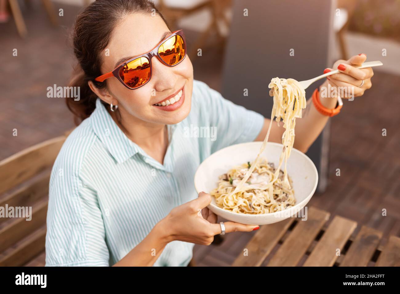 Happy asian woman eating itallian spaghetti or pasta outdoors in open ...