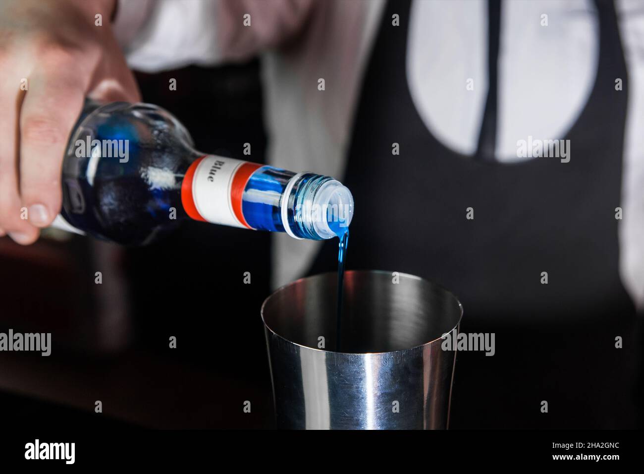 The hand of a professional bartender pours blue syrup into a tool for ...