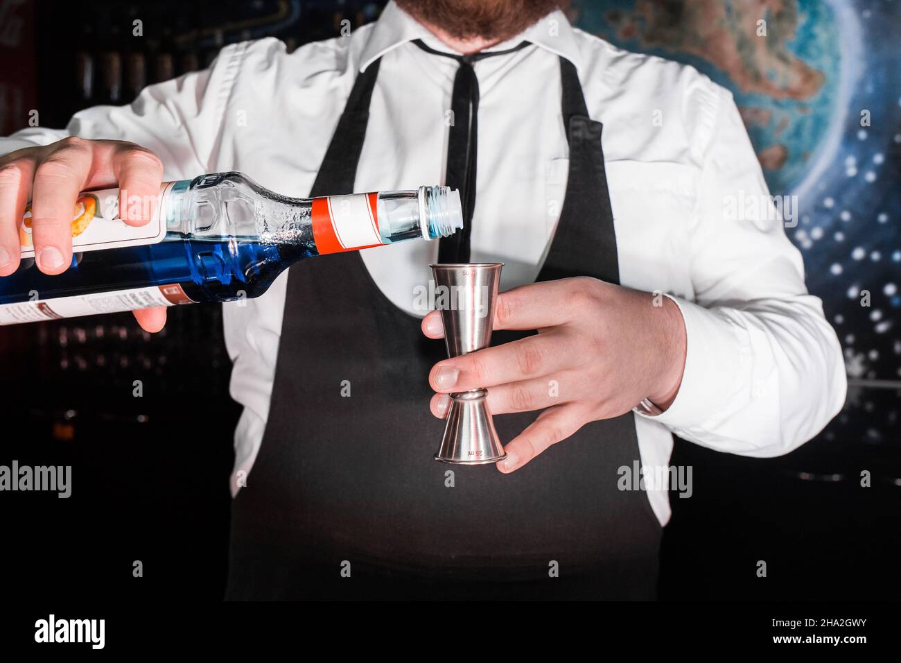 The hand of a professional bartender pours blue syrup into a tool to ...
