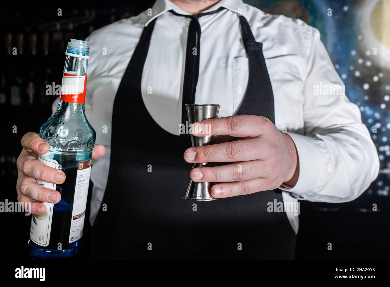 The hand of a professional bartender pours blue syrup into a tool to ...