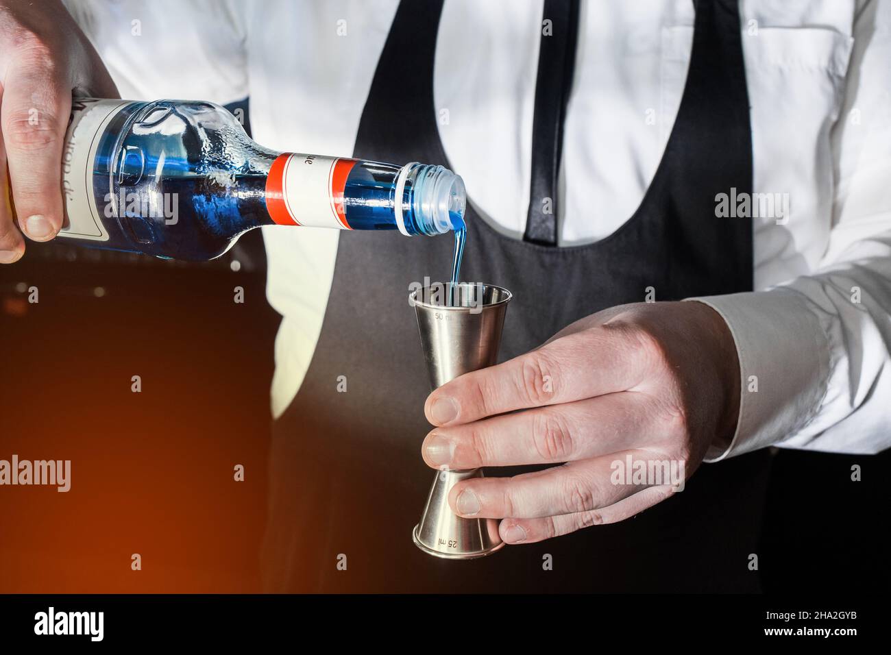 The hand of a professional bartender pours blue syrup into a tool to ...