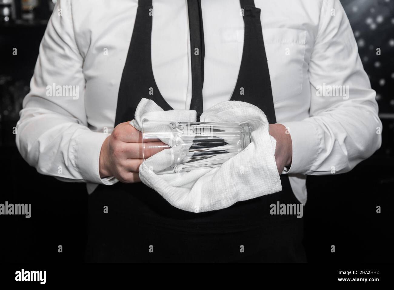 Hands of a professional bartender rub a glass glass with a white cloth ...