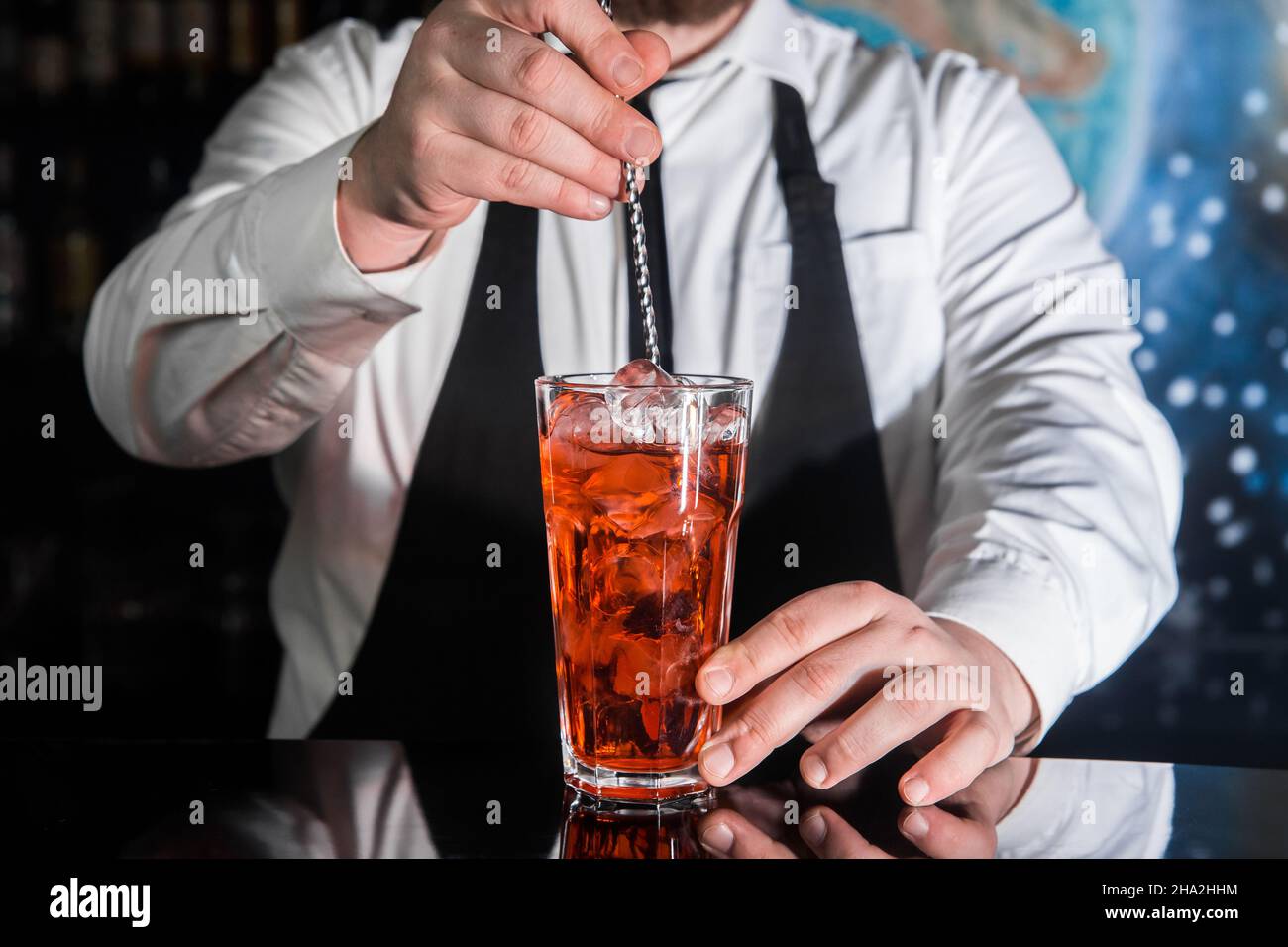 The hand of a professional bartender stirs the red syrup in an ...