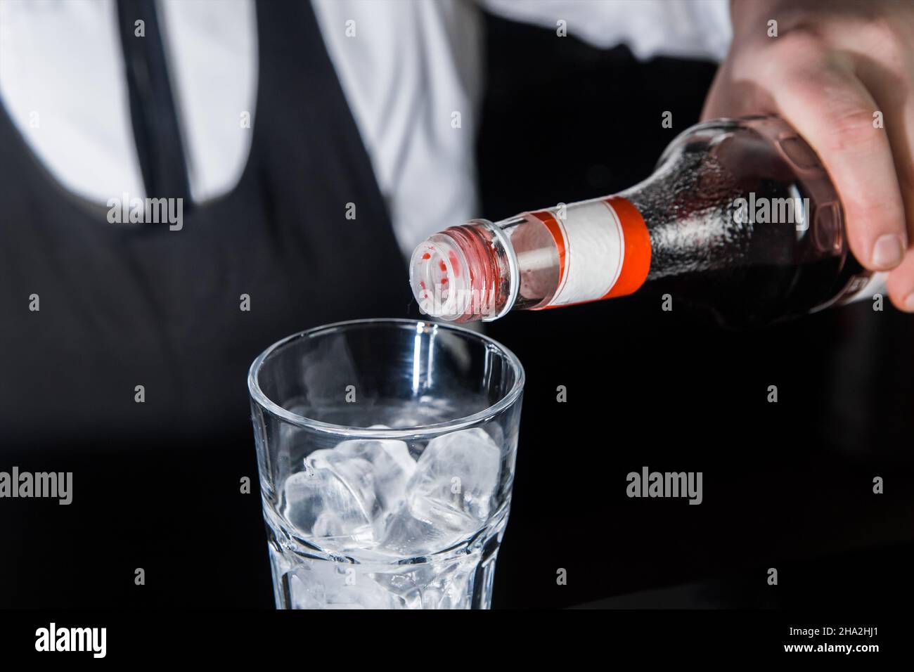 The hand of a professional bartender pours red syrup into a glass of ...