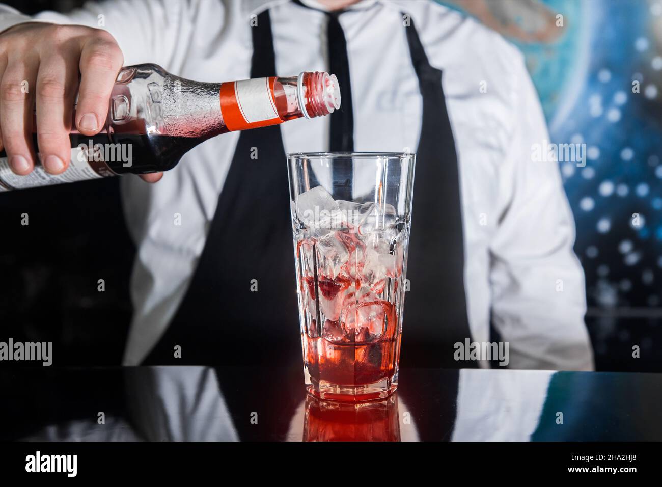 The hand of a professional bartender pours red syrup into a glass of ...