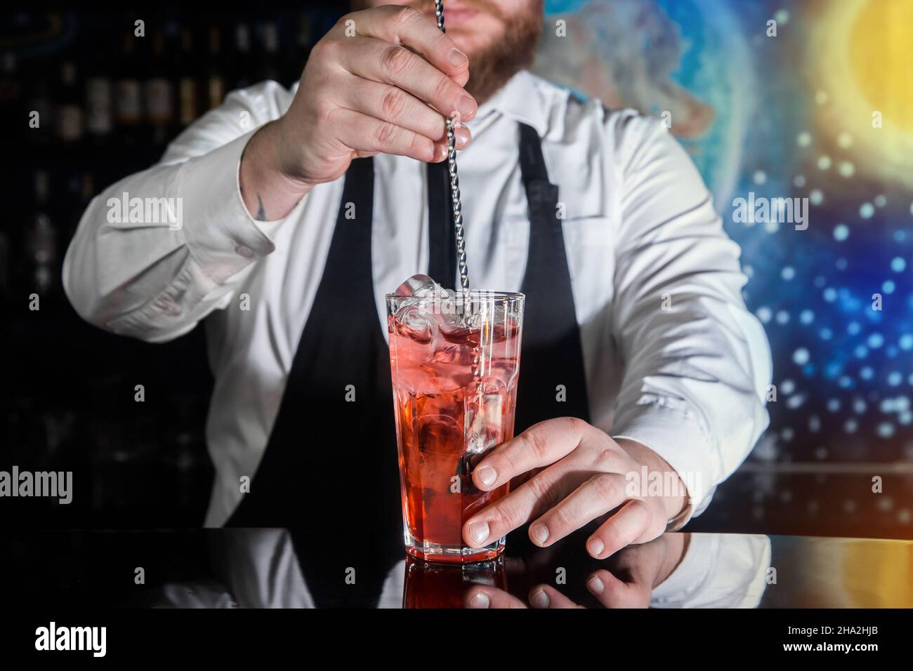 The hand of a professional bartender stirs the red syrup in an ...
