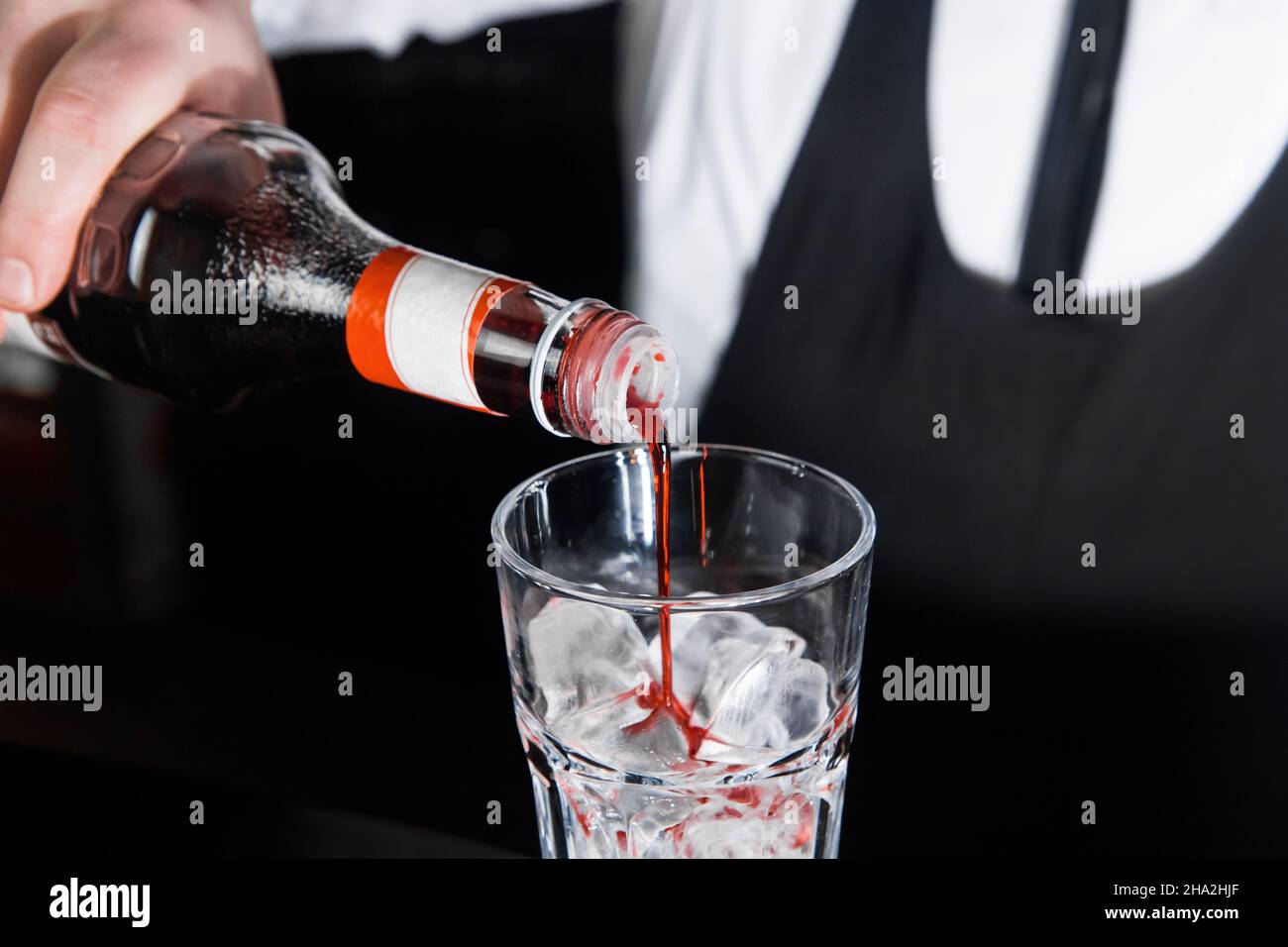 The hand of a professional bartender pours red syrup into a glass of ...