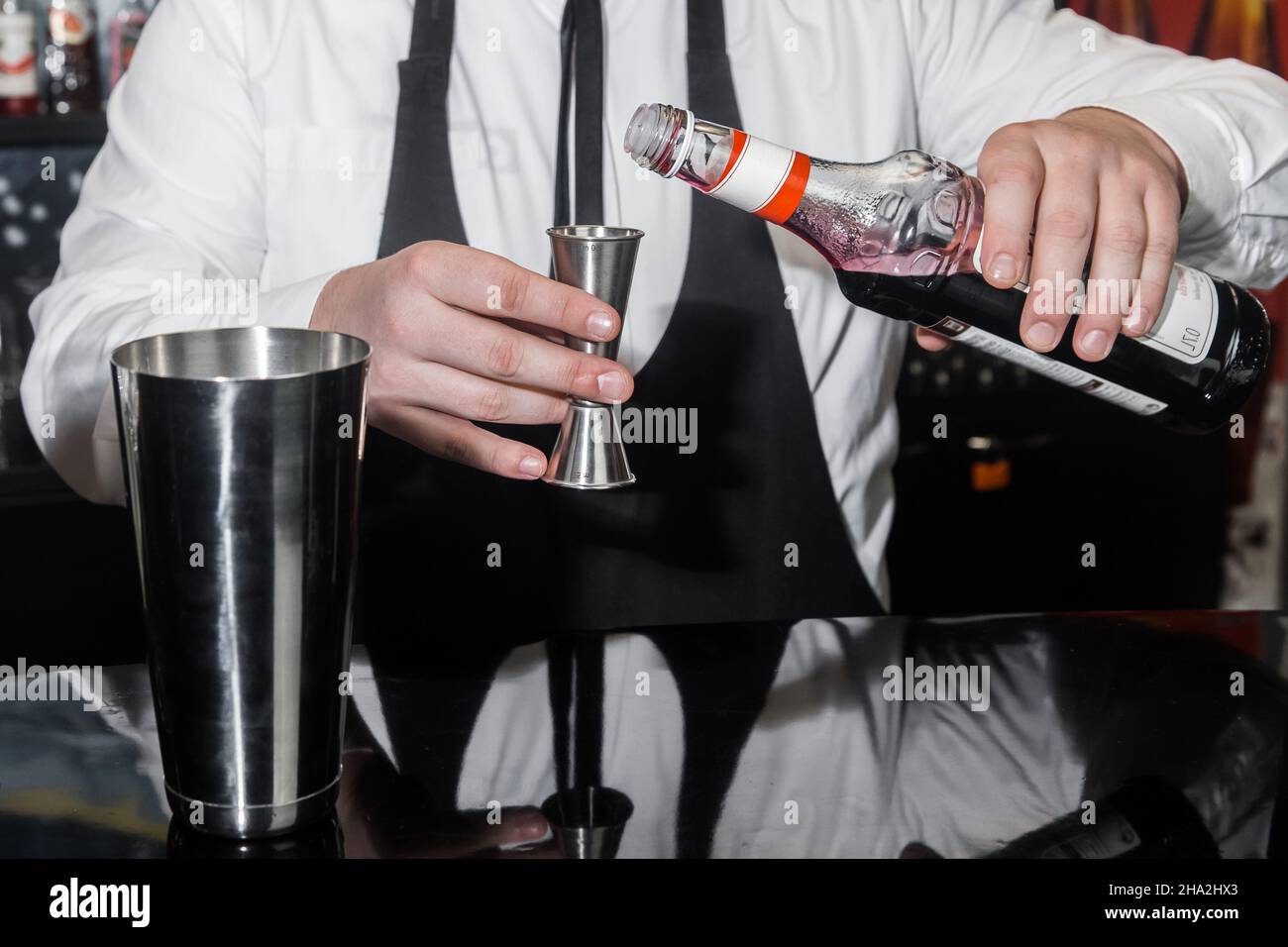 The hands of a professional bartender pour red syrup into a measuring ...