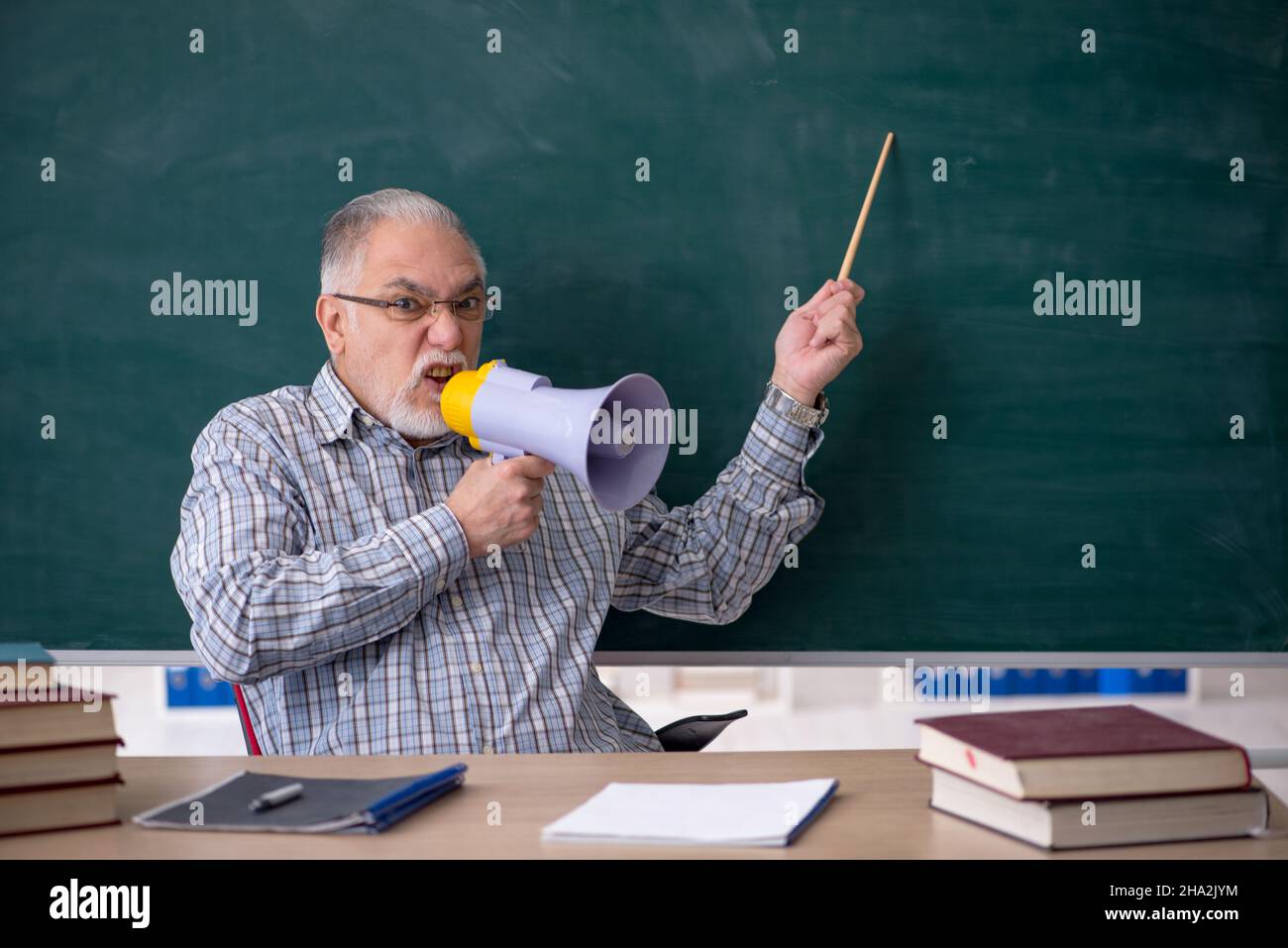 Aged male teacher holding megaphone in the classroom Stock Photo - Alamy