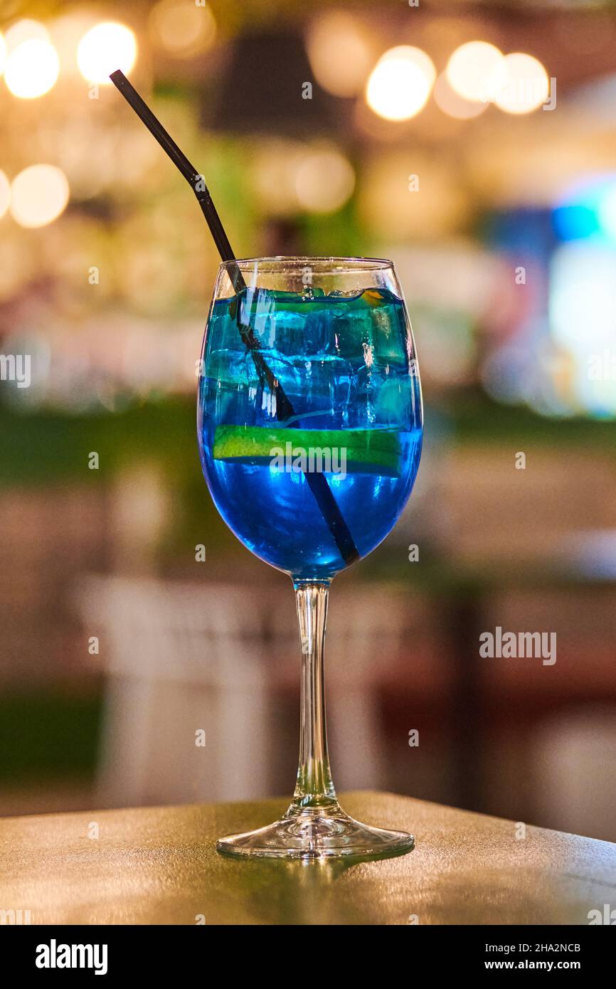 Blue Lagoon cocktail in glass with straw, night cafe light bokeh ...