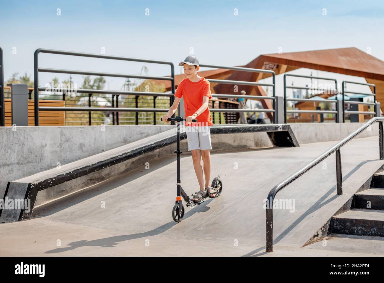 Happy teenage boy rides a kick scooter in a city skatepark with ramp ...