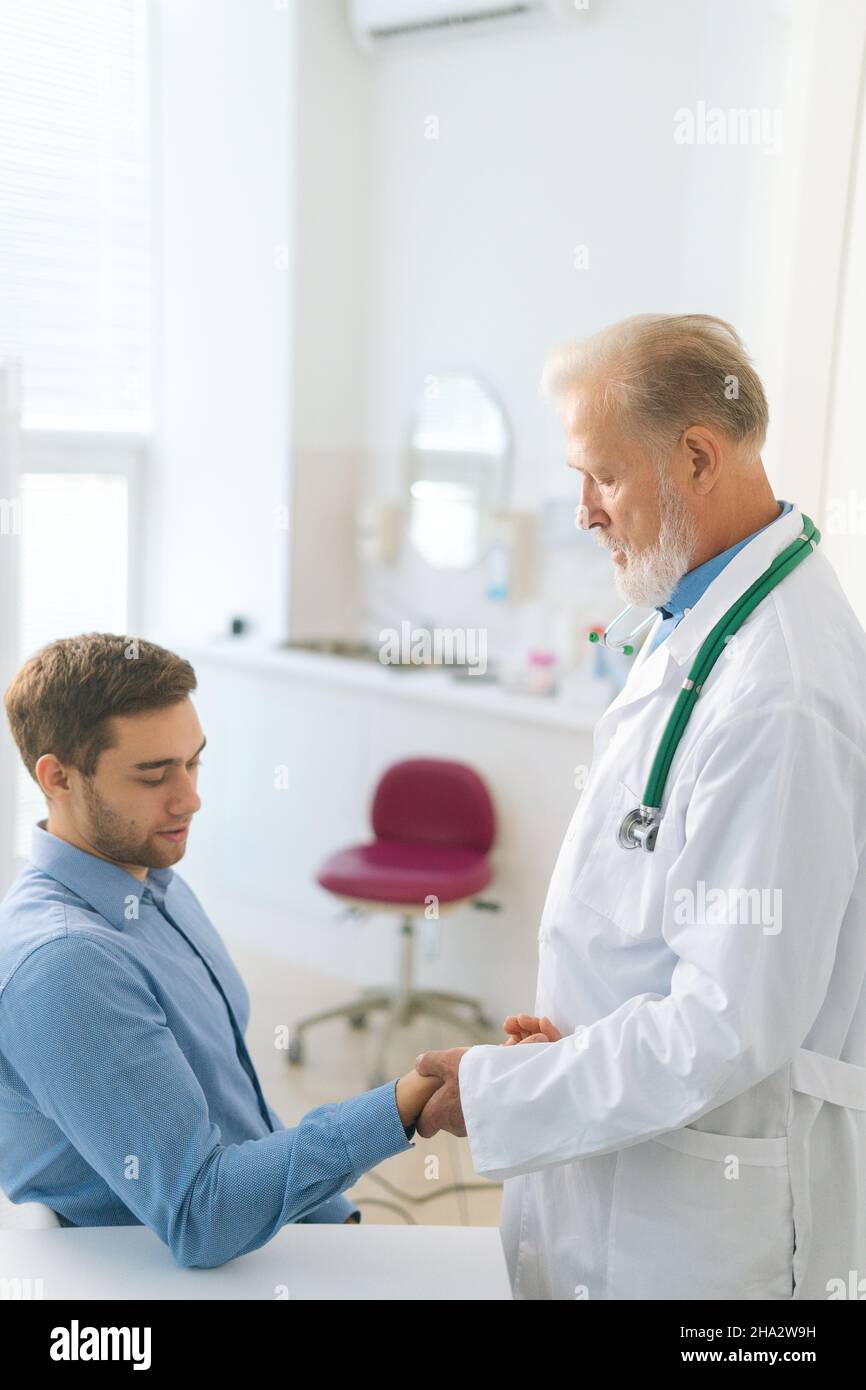 Vertical shot of standing mature male adult doctor examining hands of ...