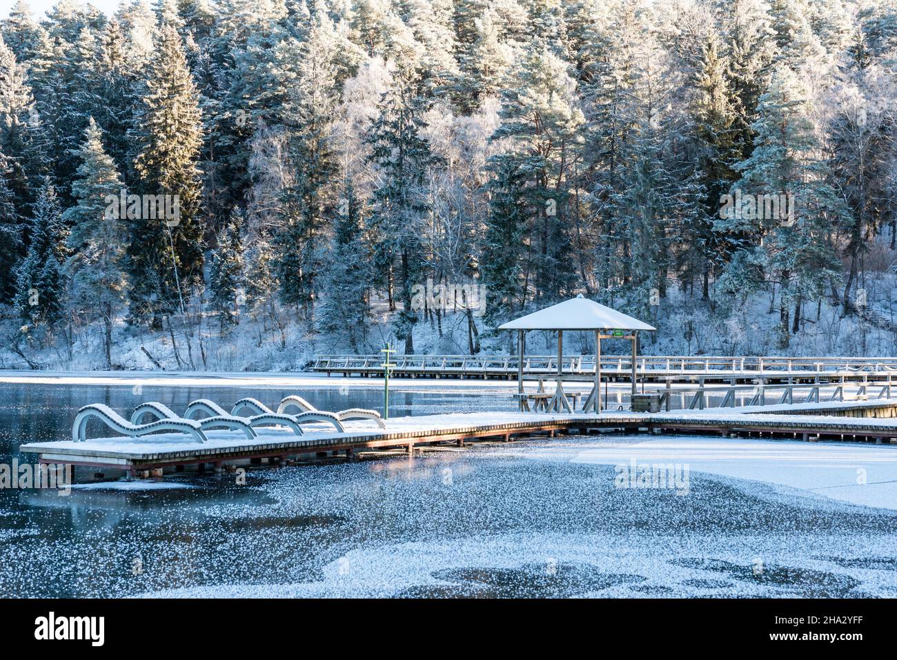 Lake beach jetty with sun beds covered in snow, frozen lake and frosted ...