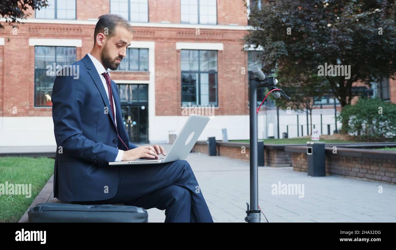 Businessman in diplomatic suit sitting on bench typing company strategy ...
