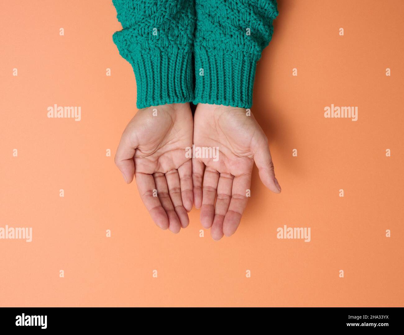 two female hands folded palm to palm on a orange background, top view ...